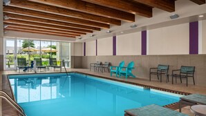 Piscina interior com vigas de madeira, paredes de vidro e áreas de estar com cadeiras e guarda-sóis.