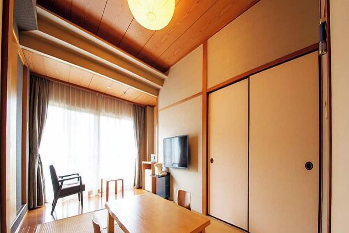 Um quarto japonês tradicional com tatames, uma mesa baixa, uma televisão e portas de correr.