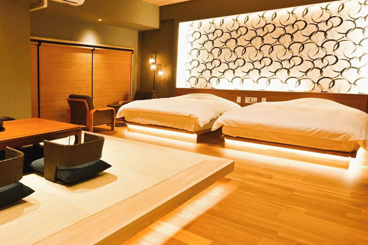 Quarto com mesa de madeira, duas cadeiras, um sofá-cama e uma janela grande com cortina estampada.