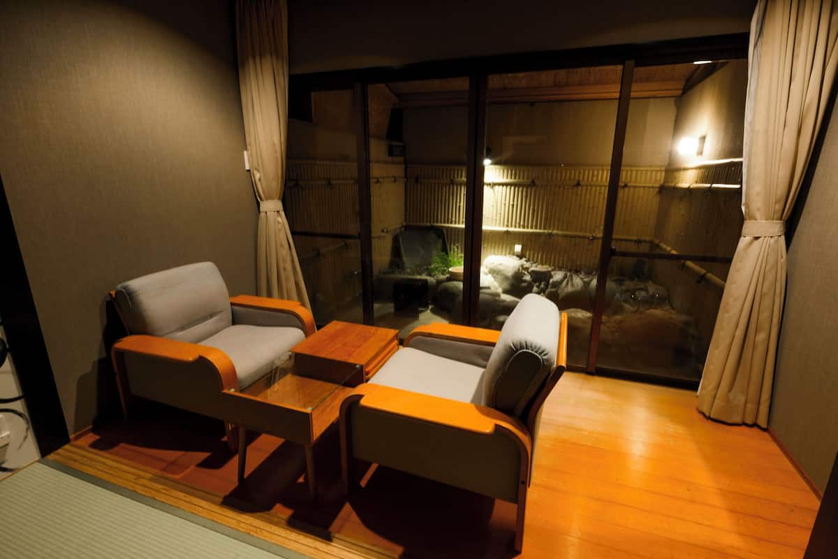 Quarto com dois sofás e uma mesa pequena, porta de correr de vidro que dá para uma varanda com vista para um jardim.