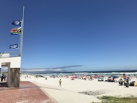 Uma praia com um mastro, pessoas e guarda-sóis.