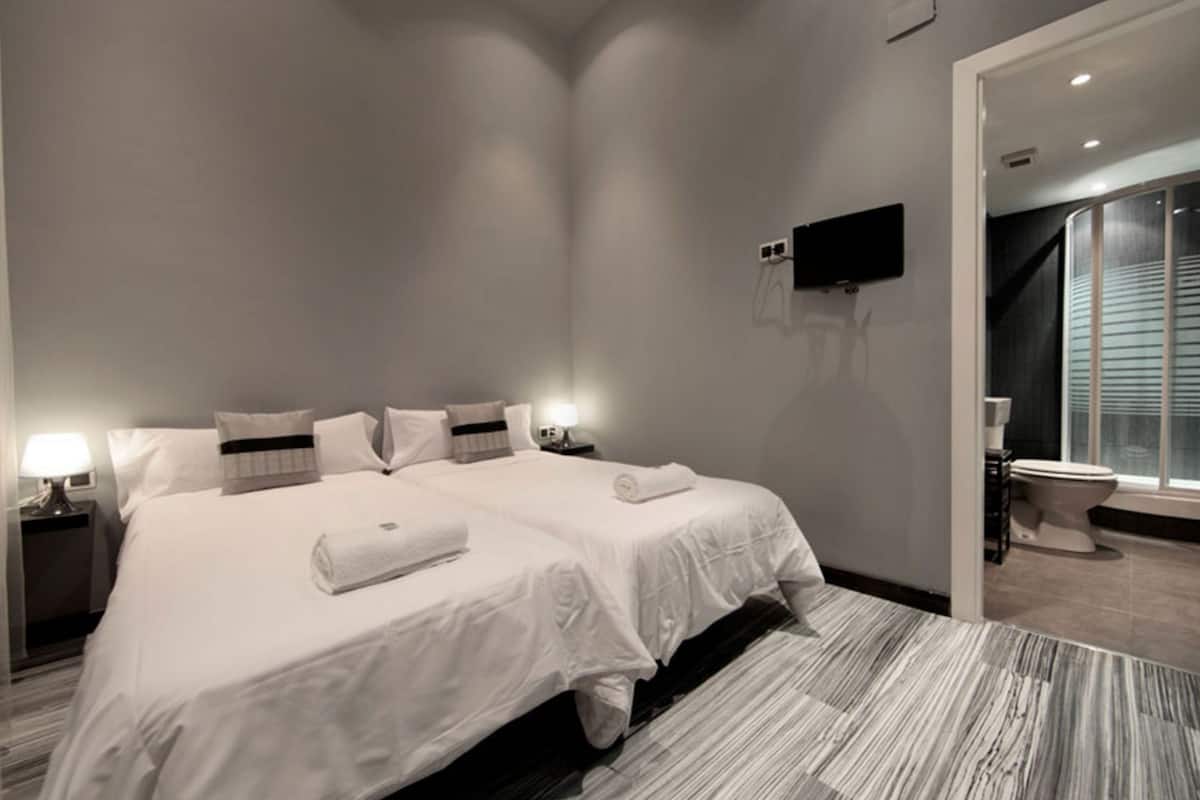 Quarto de hotel moderno com uma cama grande, televisão de tela plana na parede e banheiro separado com vaso sanitário e pia.