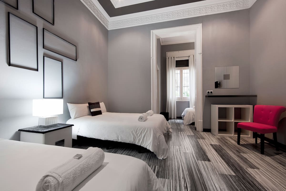 Quarto de hotel com duas camas, uma escrivaninha, uma cadeira e uma toucador com espelho.