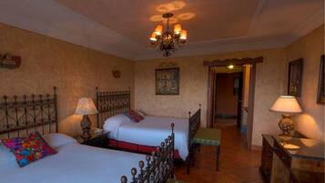 Quarto de hotel com duas camas, um candelabro, uma escrivaninha e uma cadeira.