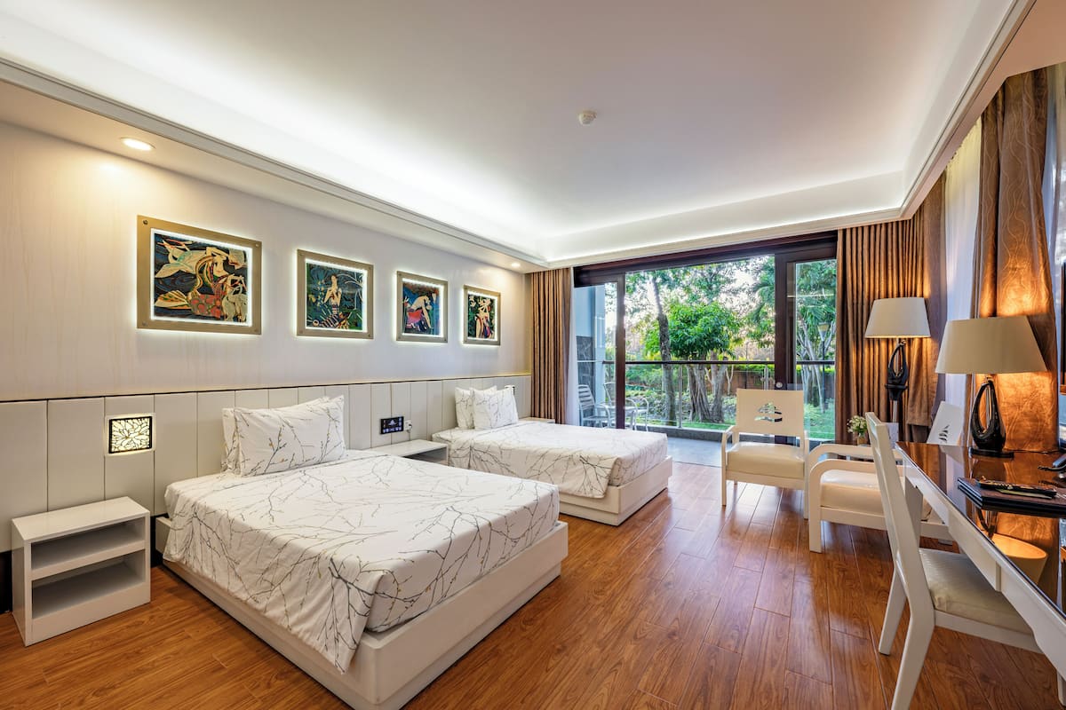 Quarto de hotel moderno com duas camas, uma escrivaninha, cadeiras e obras de arte na parede.