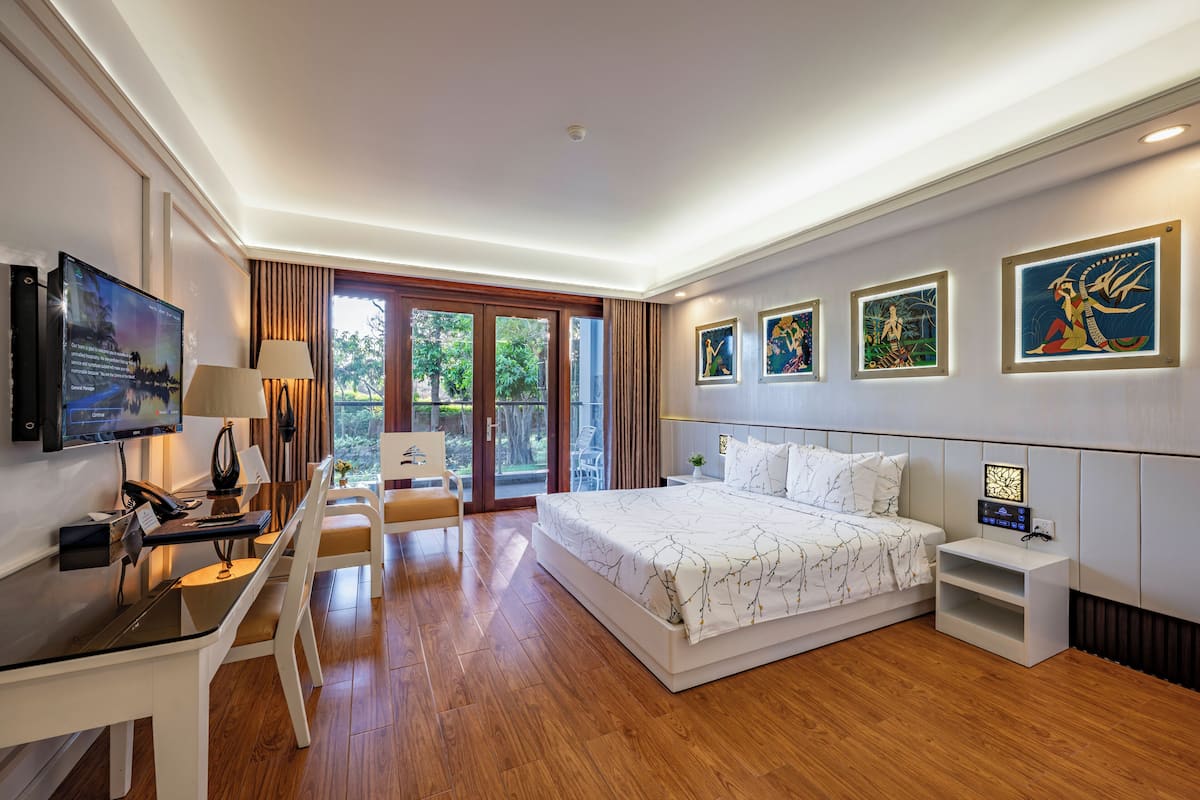 Quarto de hotel moderno com uma cama grande, uma escrivaninha com computador, uma cadeira, televisão e obras de arte nas paredes.