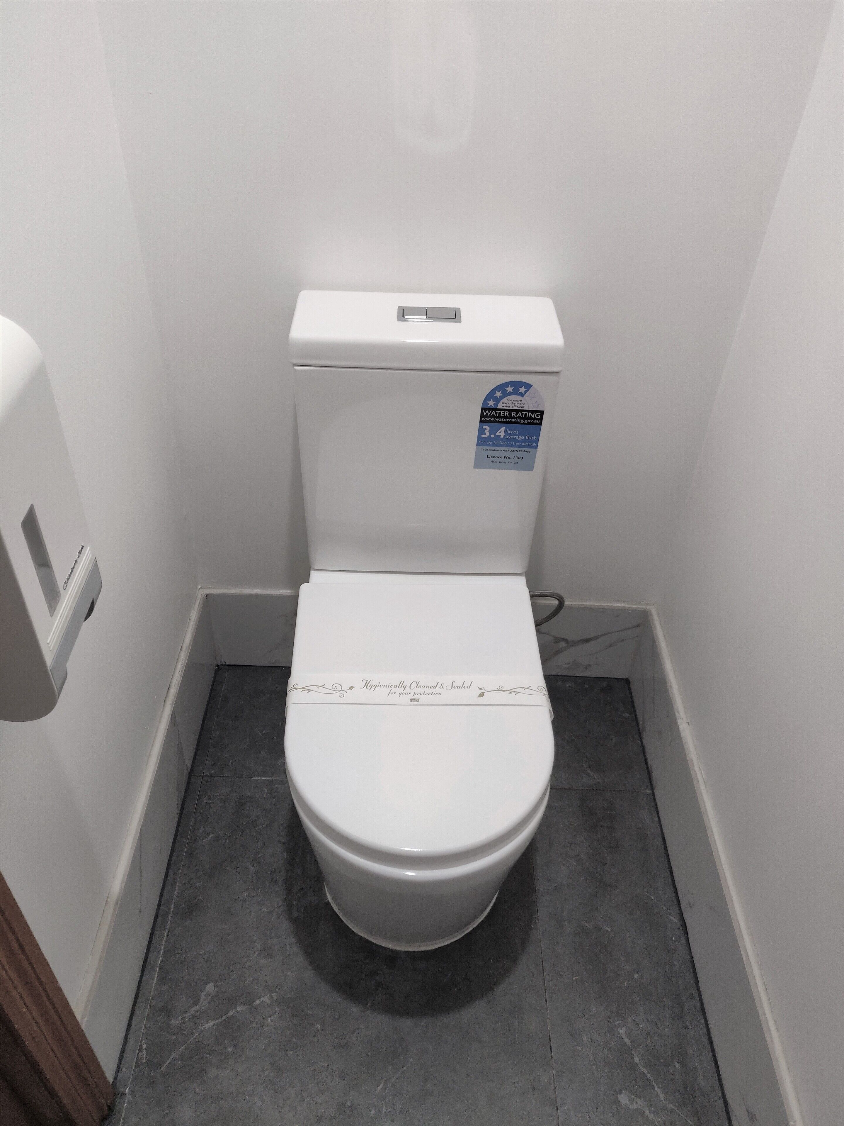 Sanitário branco com etiqueta de classificação de água, acionador de descarga e detalhes decorativos.
