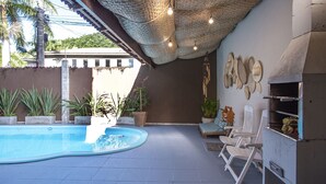 Uma piscina com espreguiçadeiras, churrasqueira e detalhes decorativos na parede.