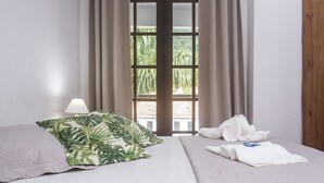 Quarto de hotel com cama, janela com cortinas, luminária e vista para o verde lá fora.