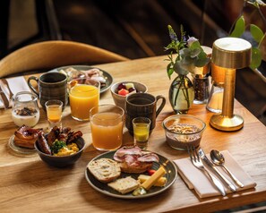 Mesa de madeira com diversos alimentos, bebidas e uma cafeteira para o café da manhã.