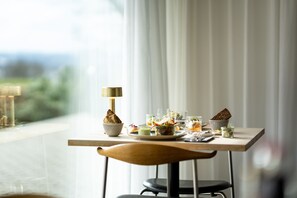 Mesa de jantar posta com pratos, copos e um abajur, localizada perto de uma janela com cortinas.