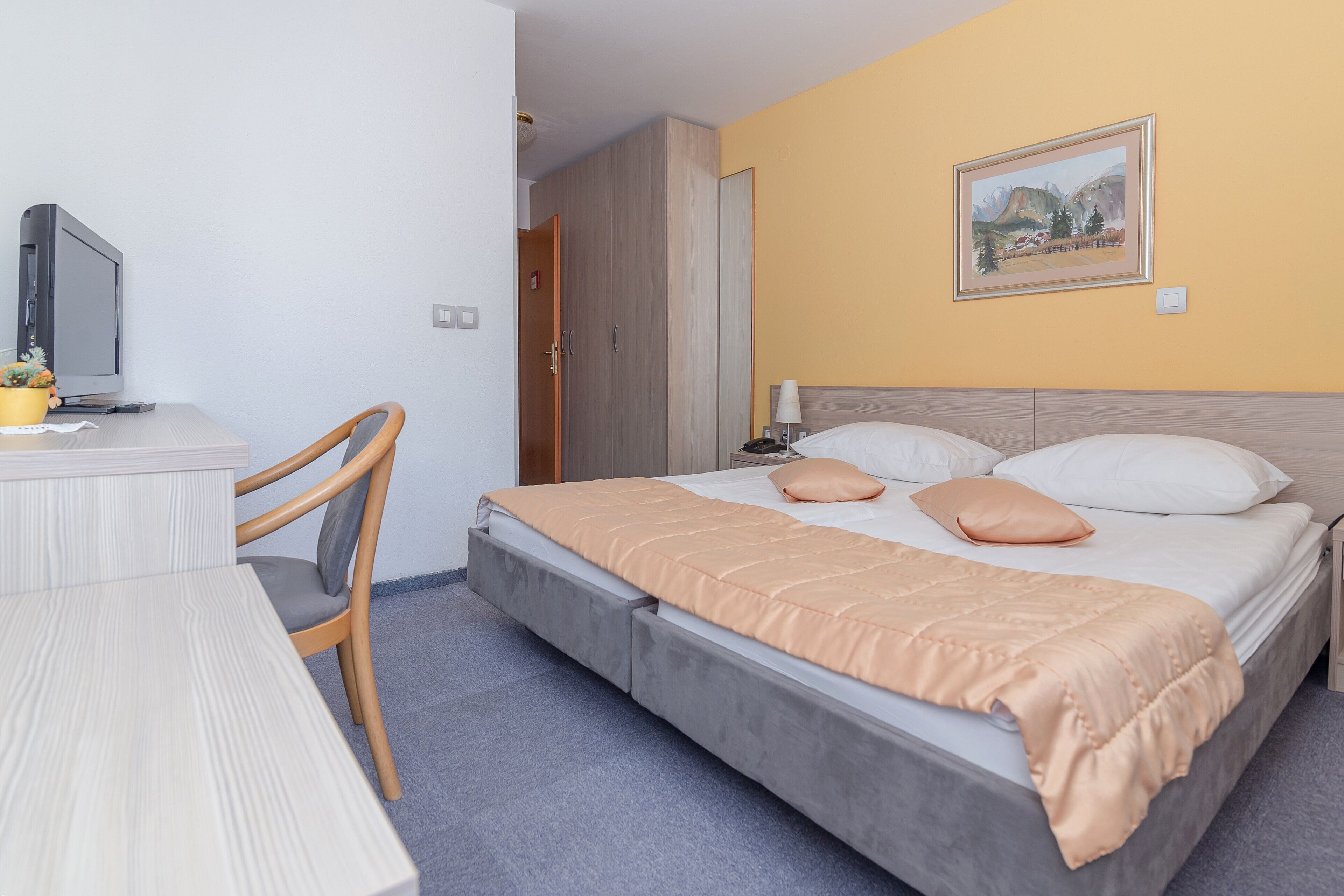 Quarto com cama, escrivaninha, cadeira e um quadro na parede.