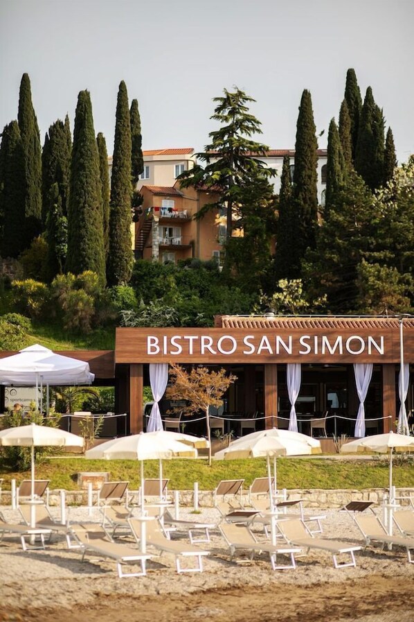 Um restaurante à beira-mar chamado Bistro Sans Simon, com mesas ao ar livre e guarda-sóis.