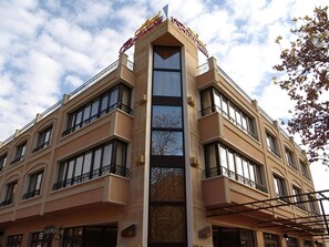 Um hotel com vários andares, fachada de vidro vertical central, varandas em cada andar e um letreiro no topo.