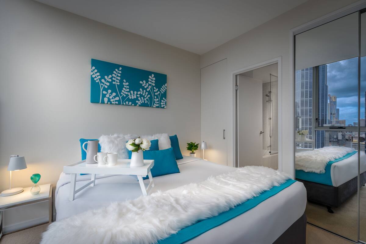 Quarto moderno com uma cama grande, uma mesa de cabeceira, um espelho e vista para a cidade.