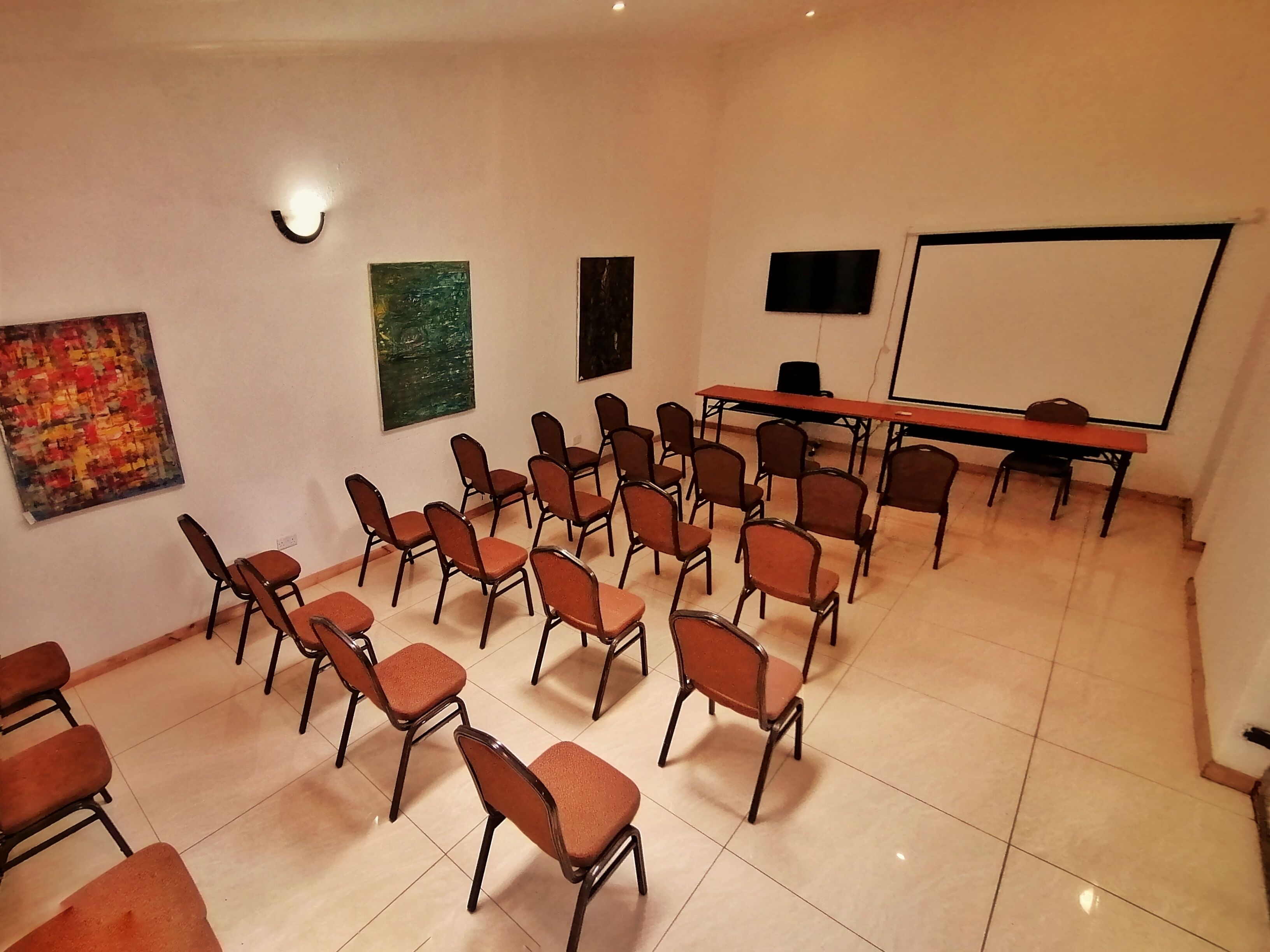 Uma sala de conferências com fileiras de cadeiras, uma tela de projetor e um quadro branco.