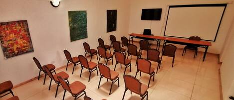 Uma sala de conferências com fileiras de cadeiras, uma tela de projetor e um quadro branco.