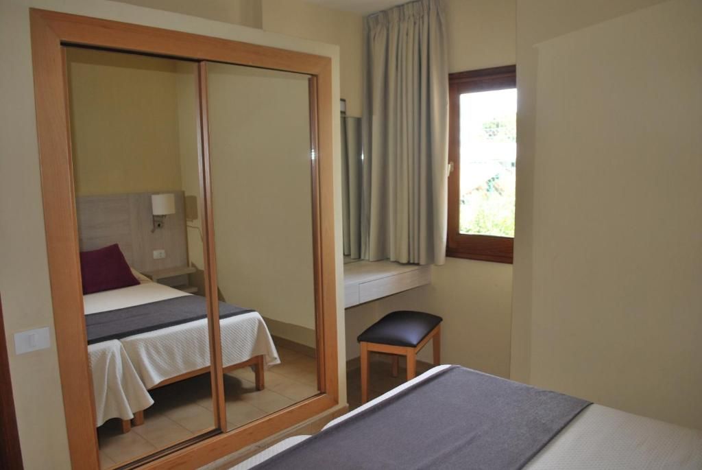 Quarto com cama, escrivaninha, cadeira, guarda-roupa e janela com cortinas.