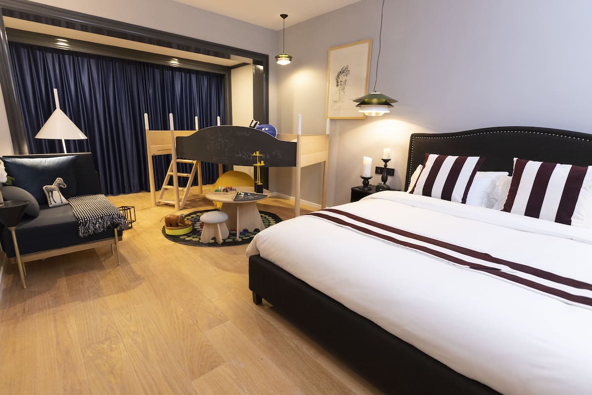 Quarto de hotel com uma cama grande, uma escrivaninha, uma cadeira, uma mesa pequena e um sofá.