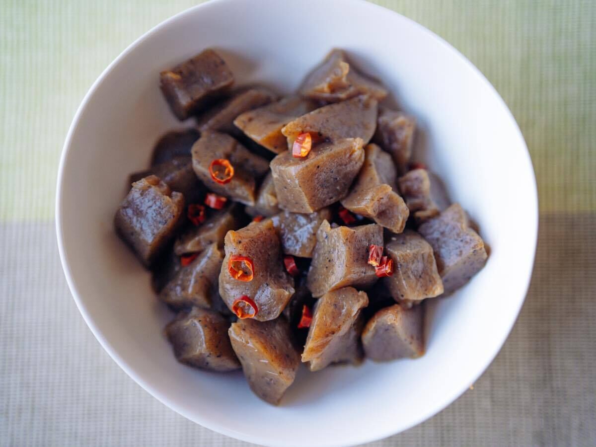 Uma tigela branca cheia de alimentos escuros, possivelmente carne, decorada com fatias de pimenta vermelha.