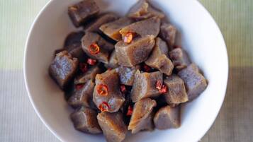 Uma tigela branca cheia de alimentos escuros, possivelmente carne, decorada com fatias de pimenta vermelha.