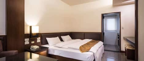 Quarto de hotel com cama, mesa de cabeceira, luminária e porta para um banheiro.