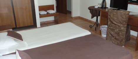 Quarto de hotel com cama, escrivaninha, cadeira, televisão e guarda-roupa.