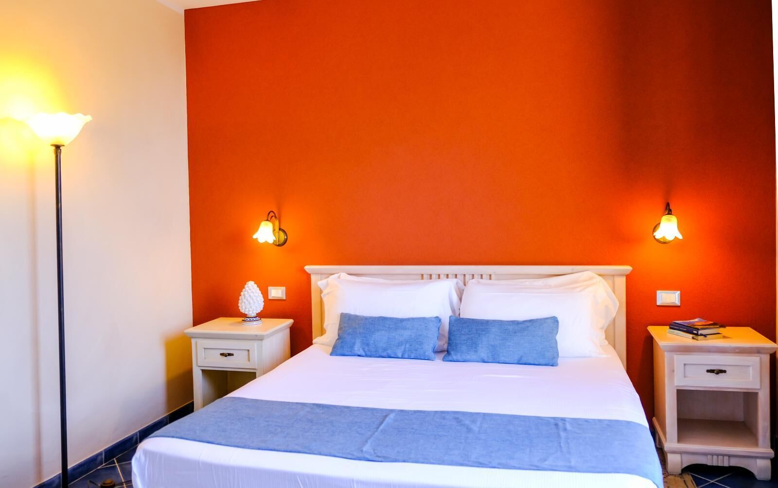 Quarto de hotel com uma cama grande, duas mesas de cabeceira e duas luminárias fixadas na parede.