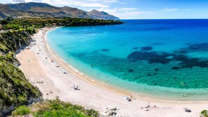 Uma praia costeira com águas turquesa cristalinas, falésias rochosas e montanhas ao fundo.