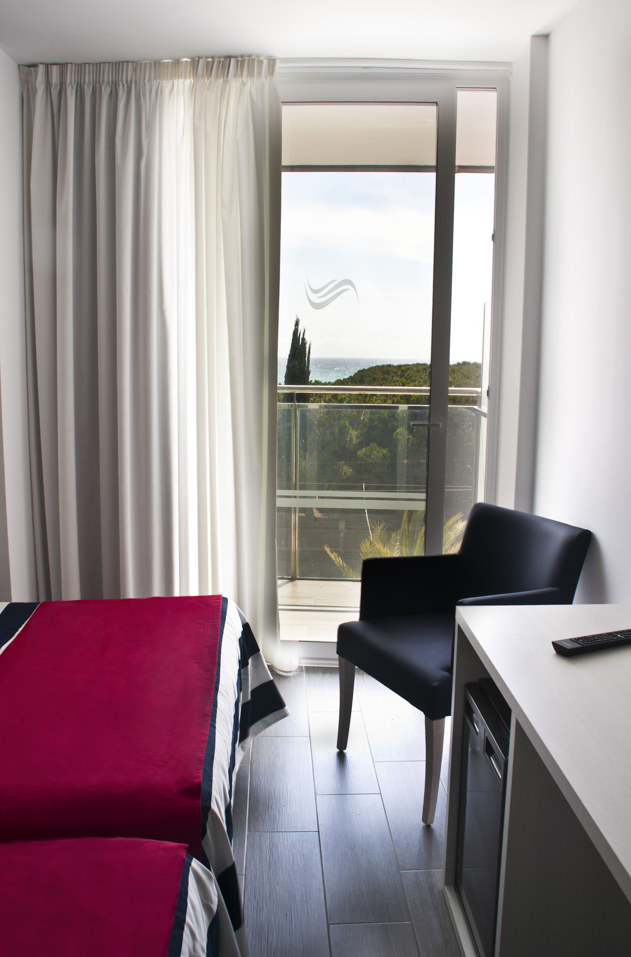 Quarto de hotel com varanda, cama, escrivaninha e cadeira.