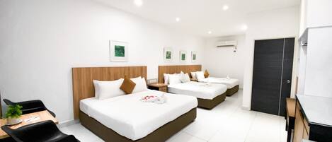 Quarto de hotel com três camas, uma mesa com cadeira e uma porta preta.