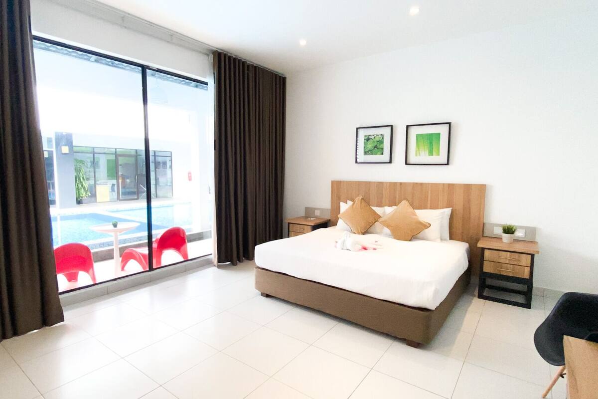 Quarto de hotel com uma cama grande, mesa de cabeceira, escrivaninha e vista para uma piscina através de uma porta de correr.