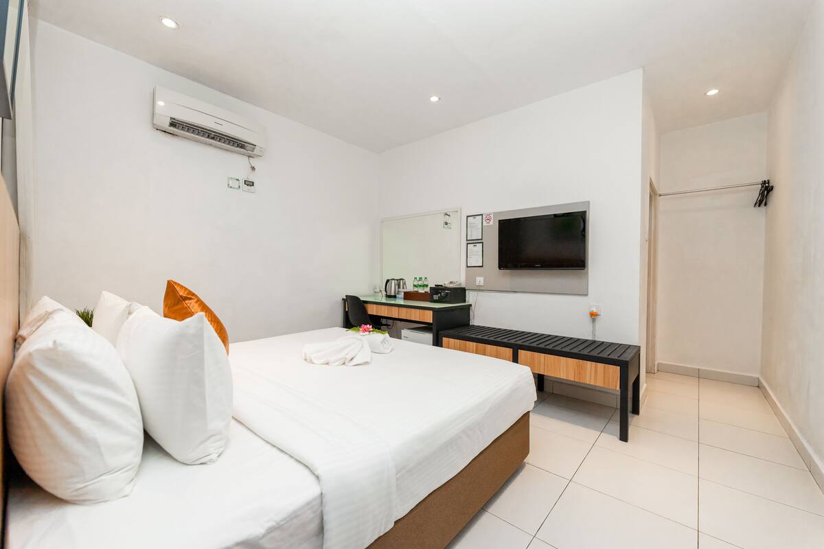 Quarto de hotel moderno com uma cama, uma escrivaninha, uma cadeira, uma TV e área de chuveiro.
