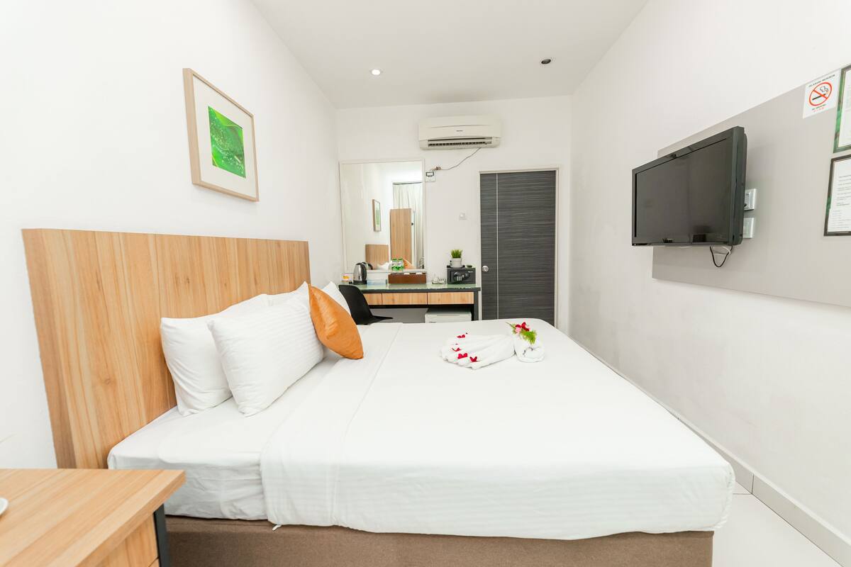 Quarto de hotel com cabeceira de madeira, roupa de cama branca, televisão de tela plana e escrivaninha com cadeira.