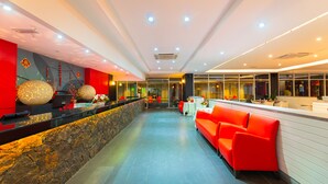 Um hall de hotel moderno com balcão de recepção, área de estar em vermelho e parede decorativa de pedra.