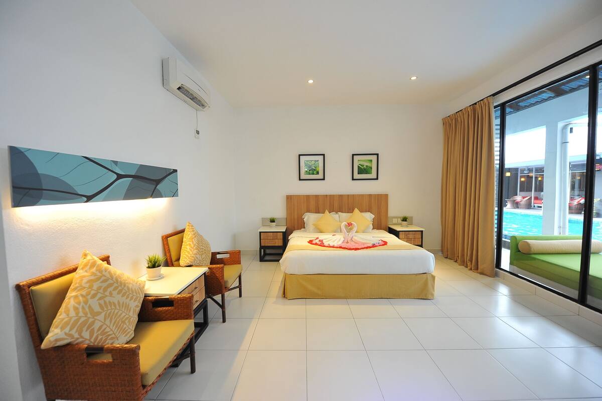 Quarto de hotel com cama, sofá, mesa de jantar e vista para uma piscina.