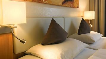 Quarto de hotel com cama, duas almofadas, mesa de cabeceira, abajur e um quadro na parede.