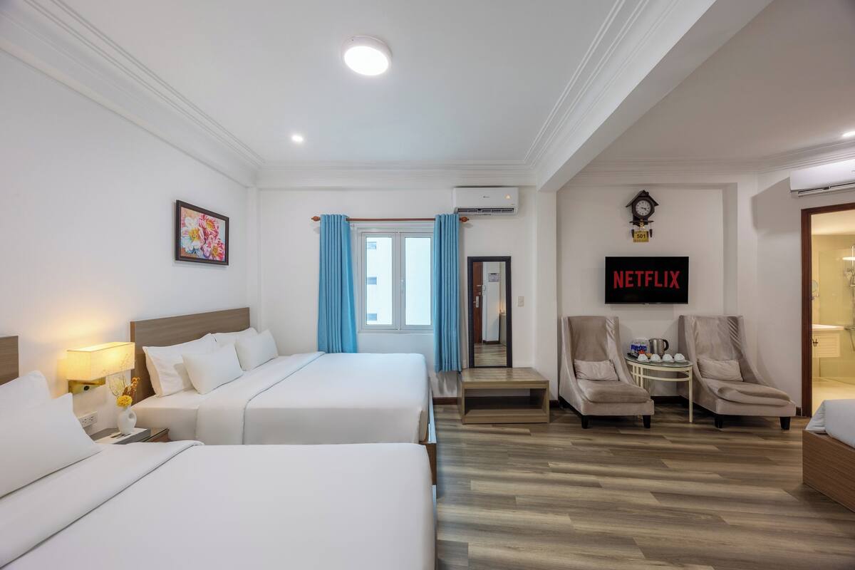 Quarto de hotel com duas camas, televisão, relógio e pequena mesa com cafeteira.