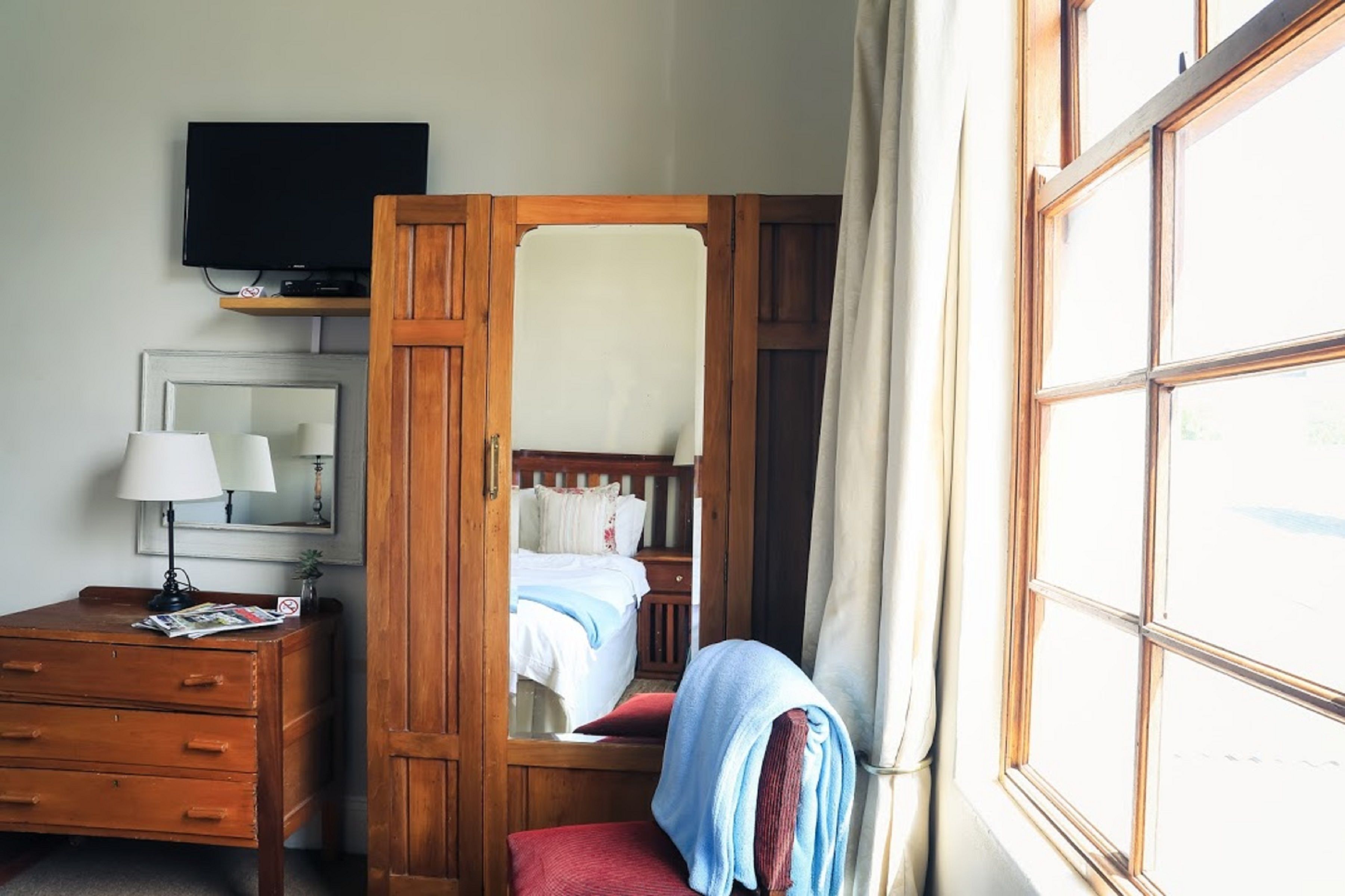 Quarto de hotel com guarda-roupa de madeira, televisão na parede, cama com manta vermelha e janela com cortinas.