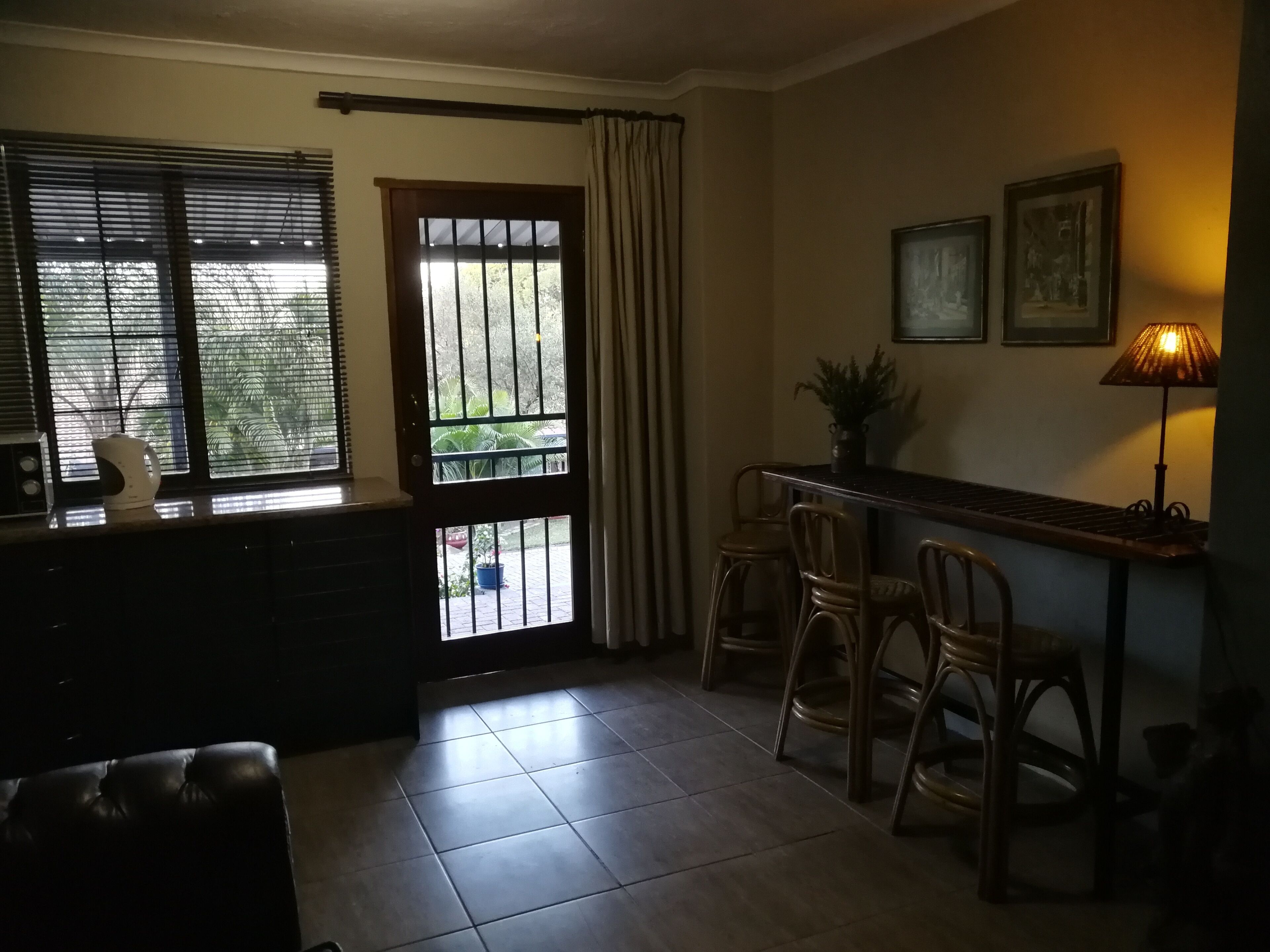 Um quarto com iluminação suave, área de cozinha, mesa de jantar com cadeiras, janela com persianas e porta com vista para o exterior.