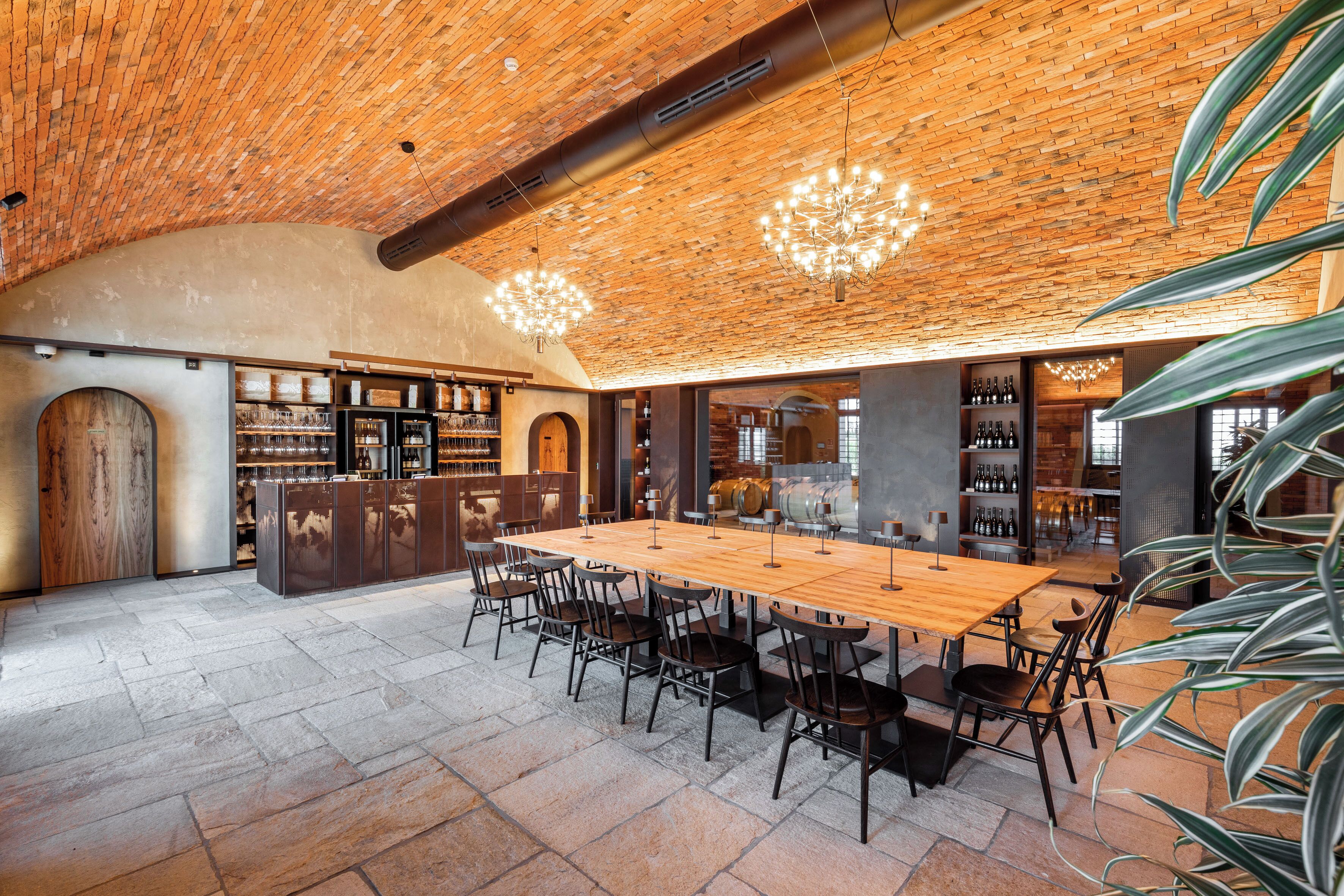 Uma sala de jantar ampla, com uma longa mesa de madeira e cadeiras, rodeada por prateleiras com garrafas e copos.