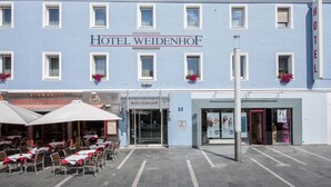 Um hotel com uma placa indicando "HOTEL WEIDENHOF" e um restaurante chamado "GAMISHA Indisches Restaurant" na frente.