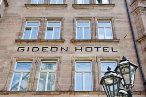 Exterior do Gideon Hotel, com fachada de pedra, várias janelas e um letreiro sobre as janelas.