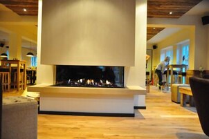 Sala de estar moderna com lareira, piso de madeira e uma pessoa ao fundo.