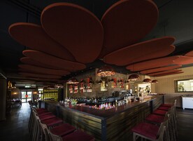 Uma área de bar com balcão central, vários arranjos de assento e um design de teto marcante.