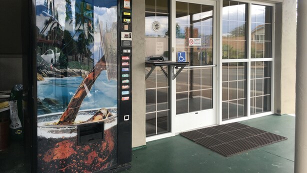 Máquina de vendas com um mural tropical, entrada acessível para cadeiras de rodas e placa de proibido fumar.