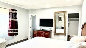 Quarto de hotel com cama, televisão, guarda-roupa e espelho.