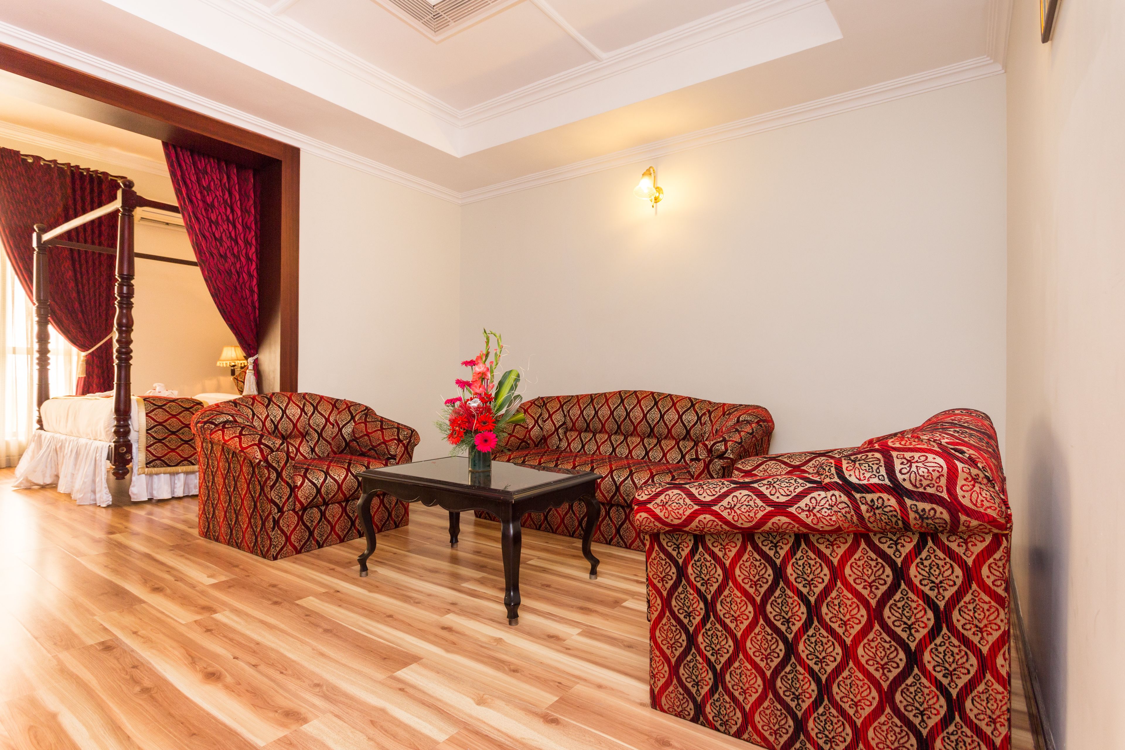 Um quarto com piso de madeira, sofás estampados, mesa de centro de vidro e cama com dossel.