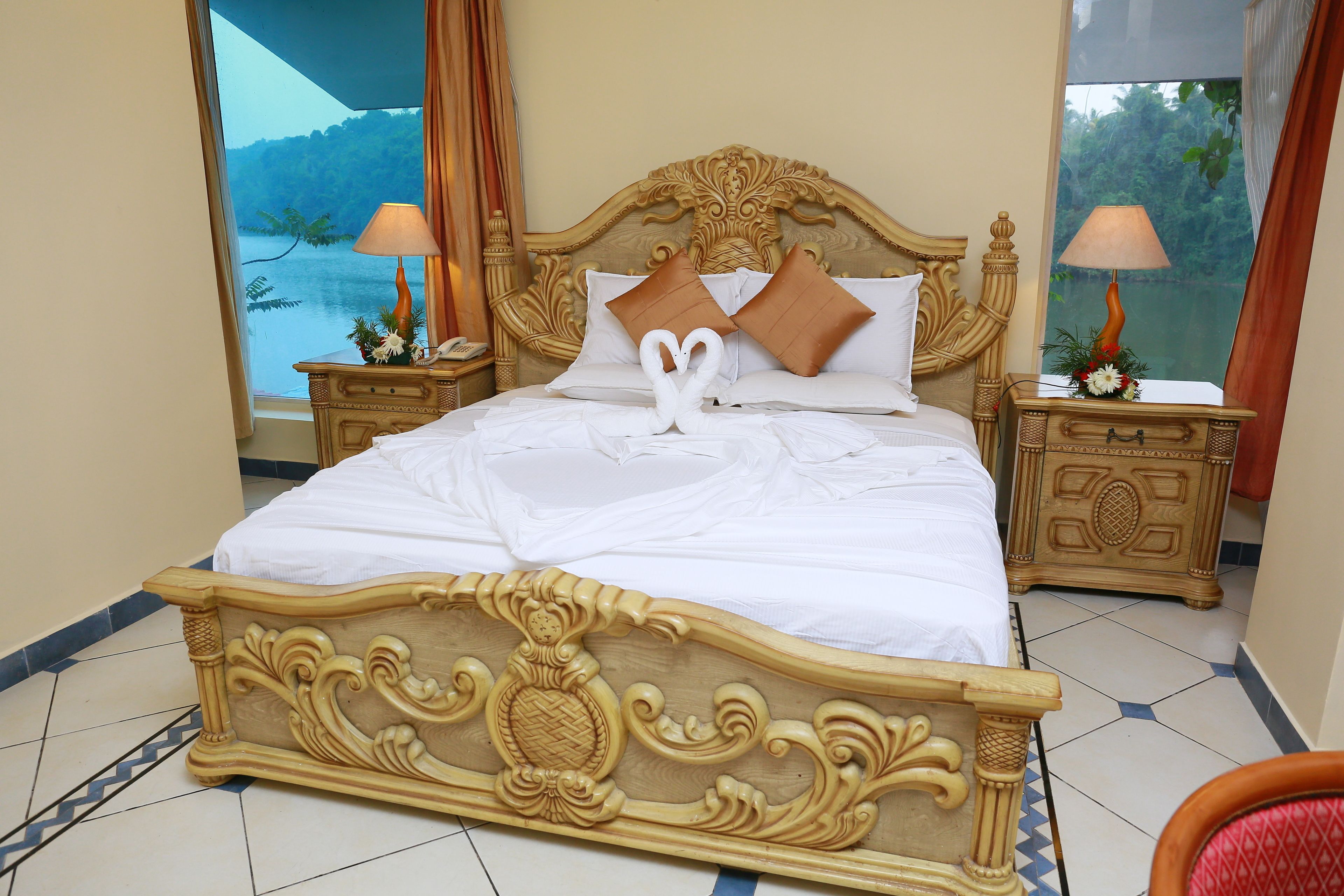 Uma cama grande com cabeceira elaborada, duas mesas de cabeceira com abajures e vista para um lago.