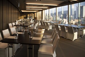 Uma sala de conferências com várias mesas e cadeiras, grandes janelas com vista para a cidade e design de interiores moderno.